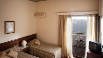 Quarto de hotel com duas camas, uma mesa pequena, televisão e varanda com vista.