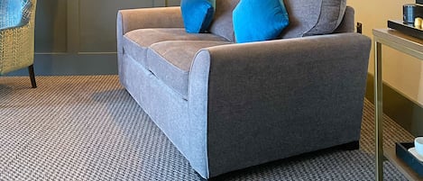 Uma sala de estar moderna com um sofá cinzento, almofadas azuis, um abajur e um quadro na parede.