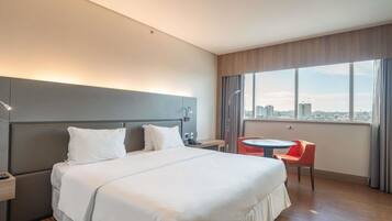 Quarto de hotel com uma cama grande, uma escrivaninha, uma cadeira e vista para a cidade.