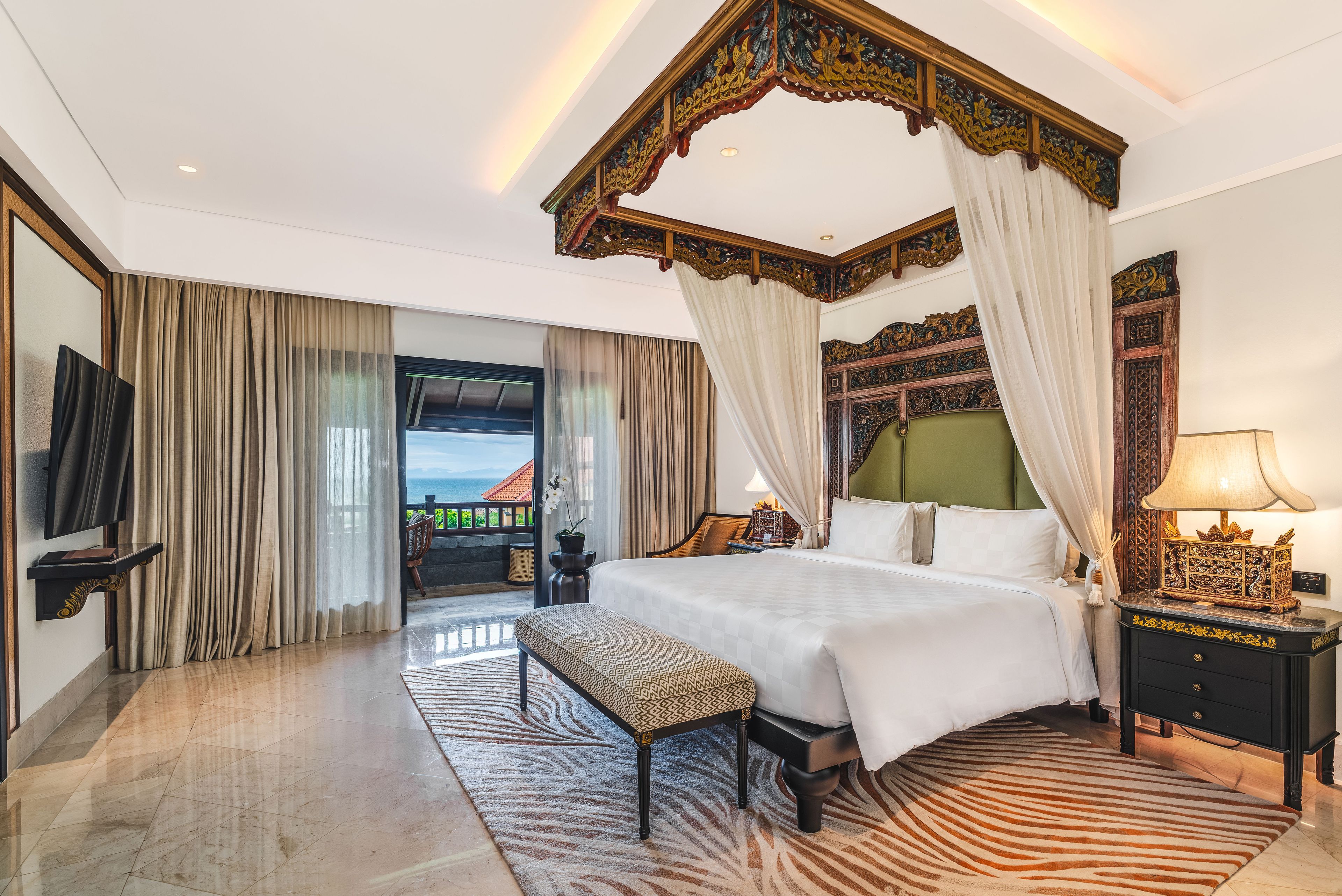 Um quarto espaçoso com cama de dossel, televisão e vista para o mar.