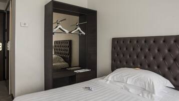 Quarto de hotel com uma cama grande, cabeceira escura, guarda-roupa com espelho e um cabideiro.