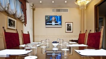 Uma sala de conferências com uma mesa grande, cadeiras vermelhas acolchoadas, uma tela de televisão e quadros nas paredes.
