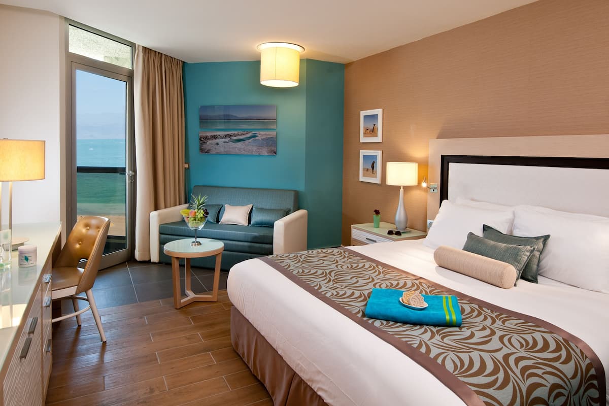 Quarto de hotel com cama, sofá, escrivaninha e vista para o mar.