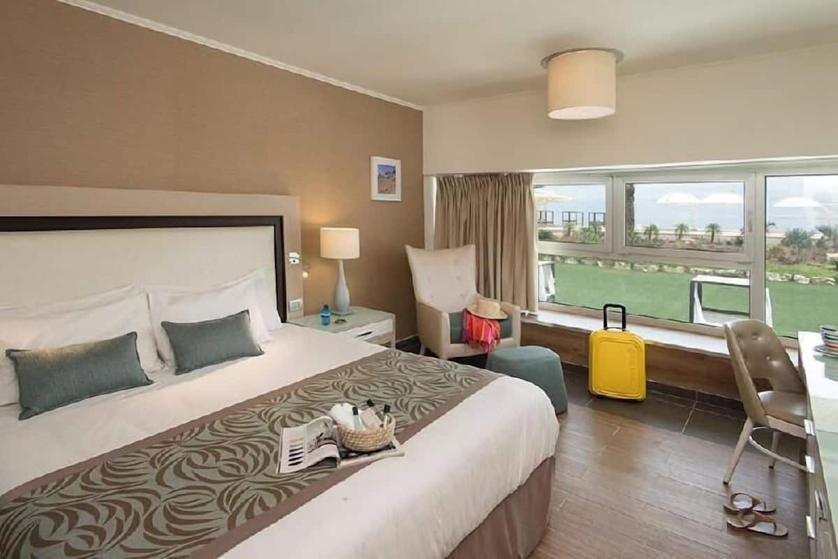 Quarto de hotel com uma cama grande, uma escrivaninha, uma cadeira, uma mala e vista para um campo de golfe.