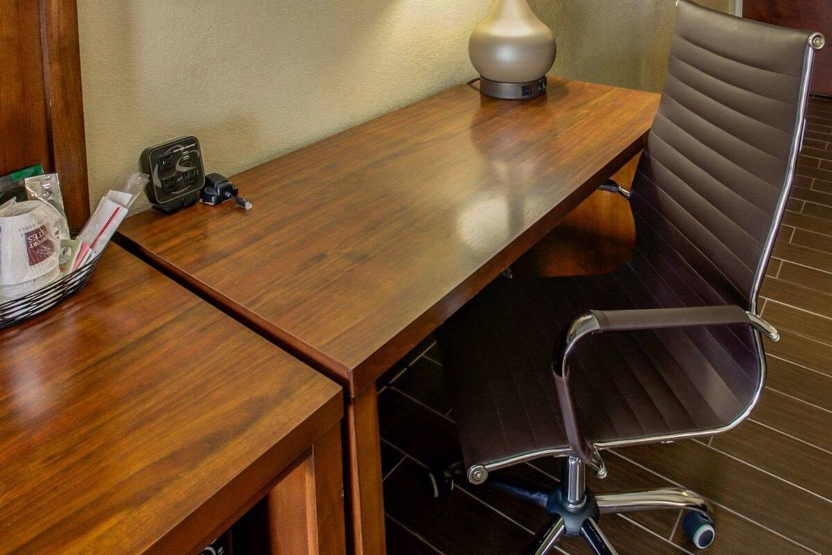 Quarto de hotel com escrivaninha de madeira, uma cadeira, abajur e telefone.