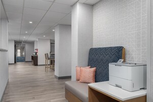 Um hall de hotel com área de estar, uma impressora e uma parede estampada.