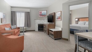 Quarto de hotel com sofá, televisão, lareira, cama e mesa de jantar.