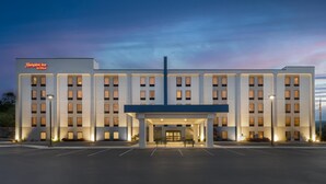 Um hotel Hampton Inn by Hilton com design moderno, com um amplo estacionamento e entrada bem iluminada.