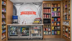 Quiosque de autoatendimento com lanches, artigos diversos e máquinas de bebidas geladas, além de prateleiras com vários petiscos e salgadinhos.
