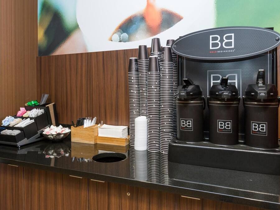 Uma área de recepção de hotel com painel de parede de madeira, balcão com pratos empilhados, guardanapos e um espaço com café, incluindo dispensadores da marca.