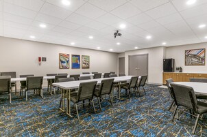 Uma sala de conferências com mesas, cadeiras, projetor e obras de arte nas paredes.