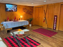 Quarto de hotel com uma cama, televisão, placa de boas-vindas e piso de madeira.