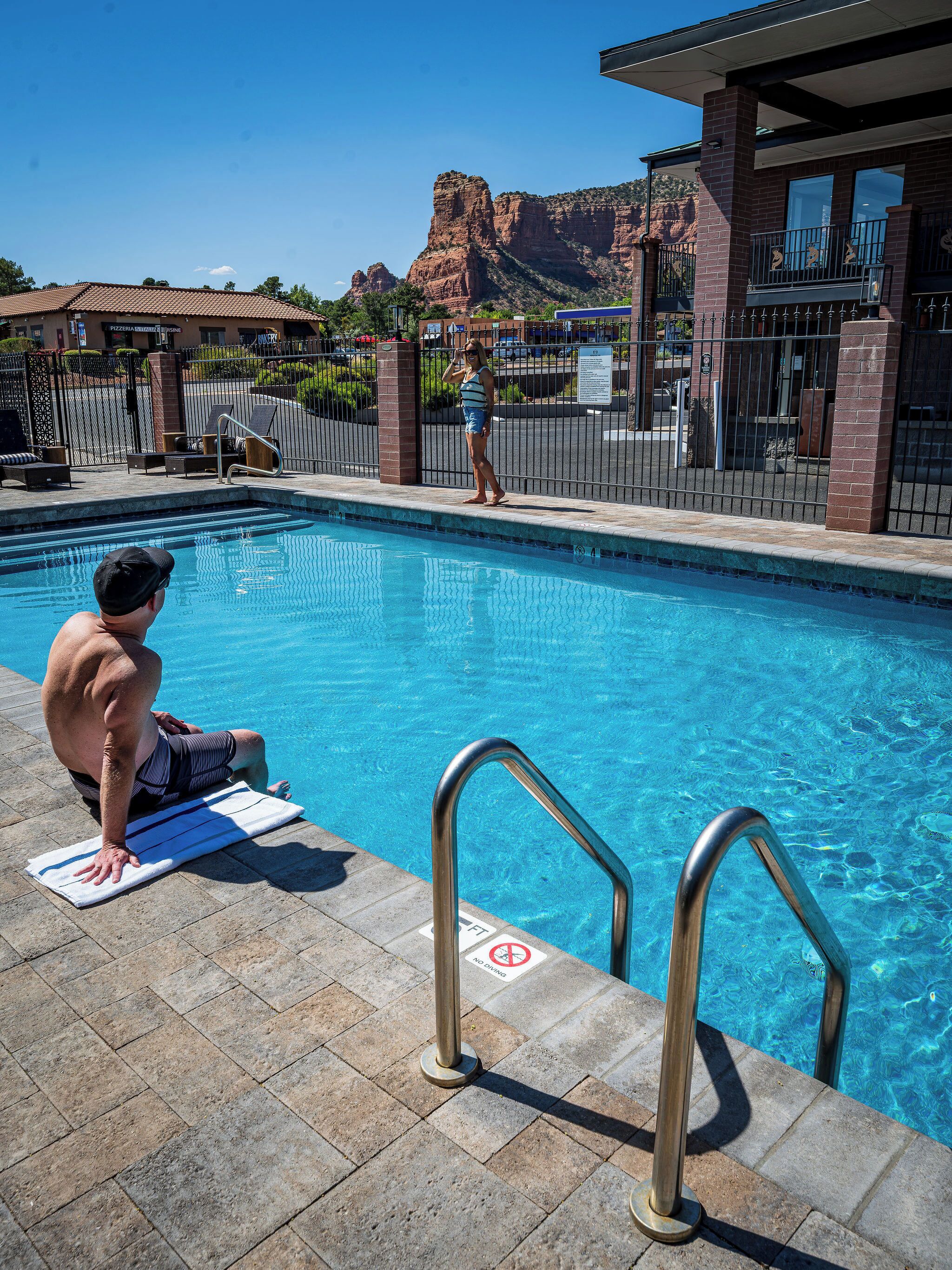 Uma piscina com grades de metal, uma toalha na borda e uma pessoa sentada sobre uma toalha.