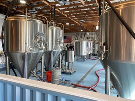 Uma cervejaria com tanques e mangueiras de aço inoxidável, vigas de madeira no teto e uma bandeira americana.