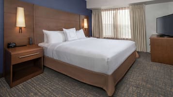 Quarto de hotel com uma cama grande, mesa de cabeceira, televisão e janela com cortinas.