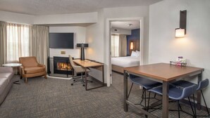 Quarto de hotel com cama, escrivaninha com cadeira, sofá, televisão e lareira.