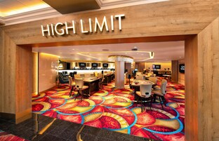 Um saguão de hotel com um aviso 'HIGH LIMIT', um carpete estampado e uma área de estar com mesas e cadeiras.