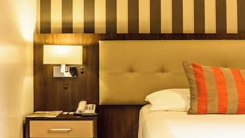 Quarto de hotel com cama, mesa de cabeceira, abajur e telefone.
