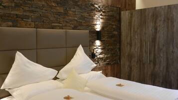 Quarto de hotel com parede de destaque em pedra, cabeceira acolchoada e cama bem arrumada com roupa de cama branca e almofadas decorativas.