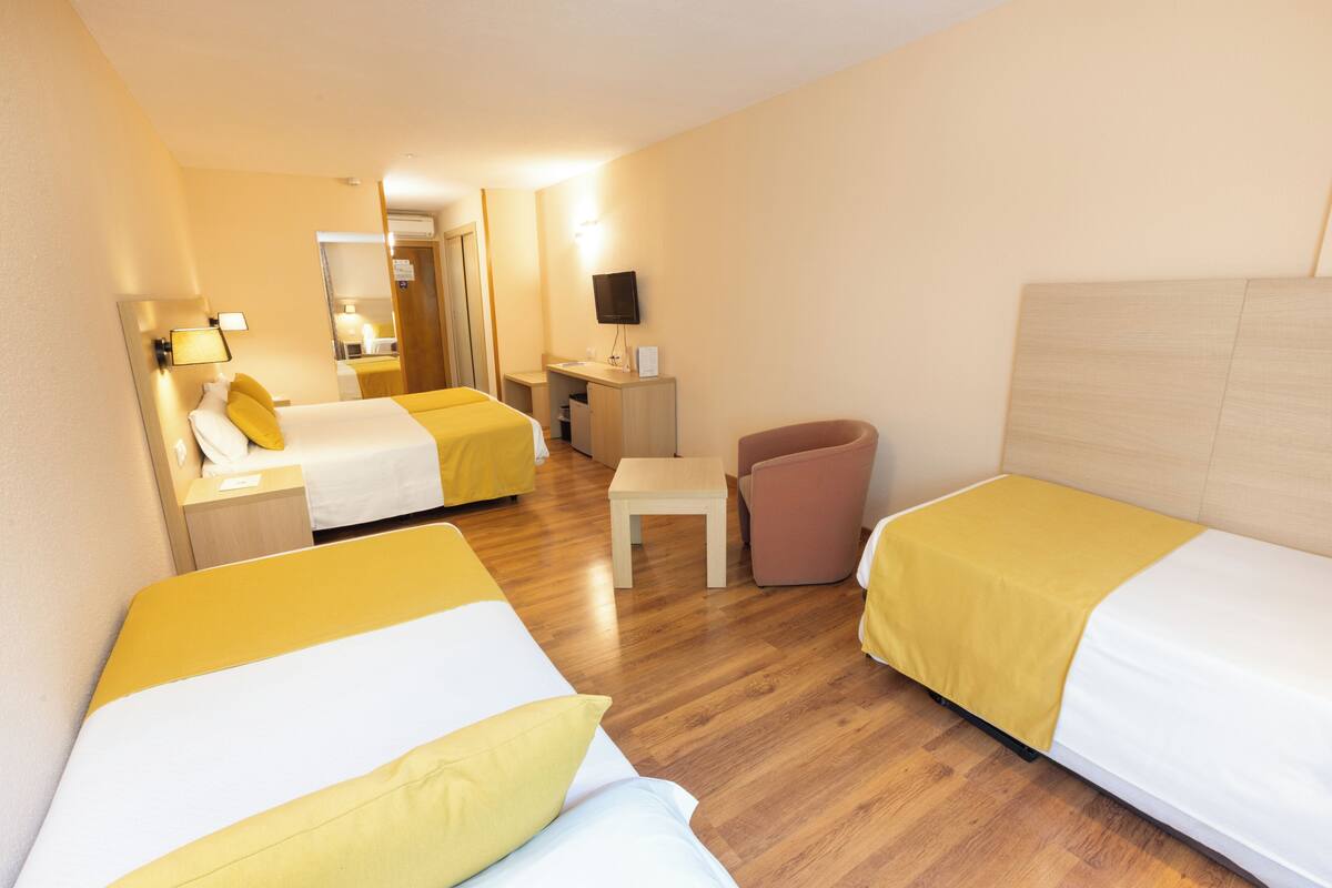 Quarto de hotel com duas camas, uma escrivaninha, uma cadeira, um espelho e uma televisão.
