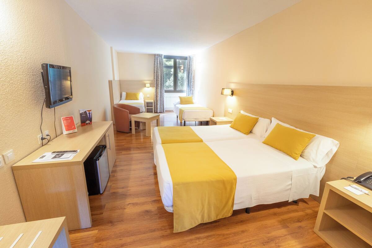 Quarto de hotel com cama, escrivaninha, cadeira e televisão.