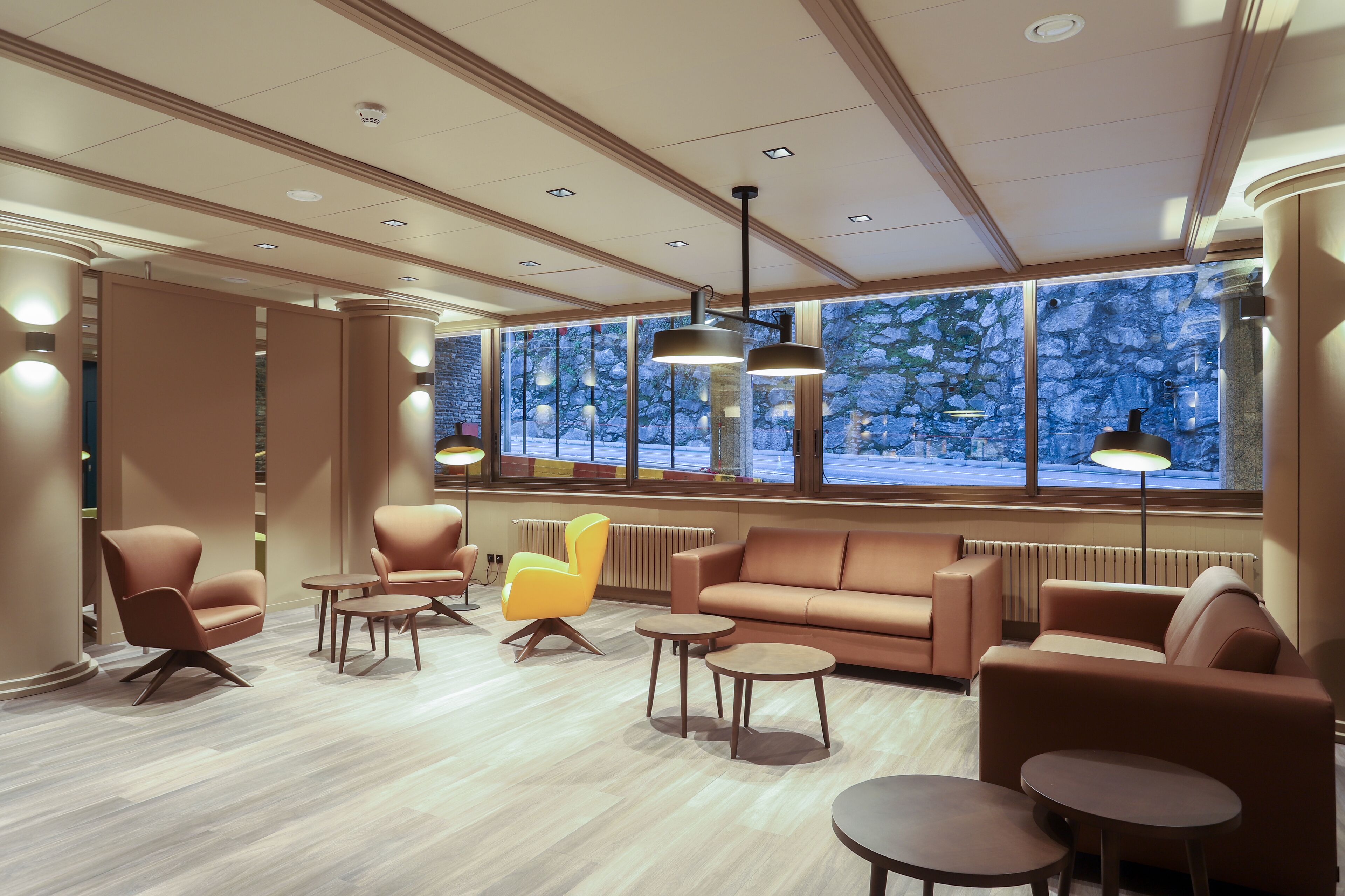 Um lobby moderno com sofás de couro, mesas redondas e grandes janelas com vista para uma paisagem coberta de neve.
