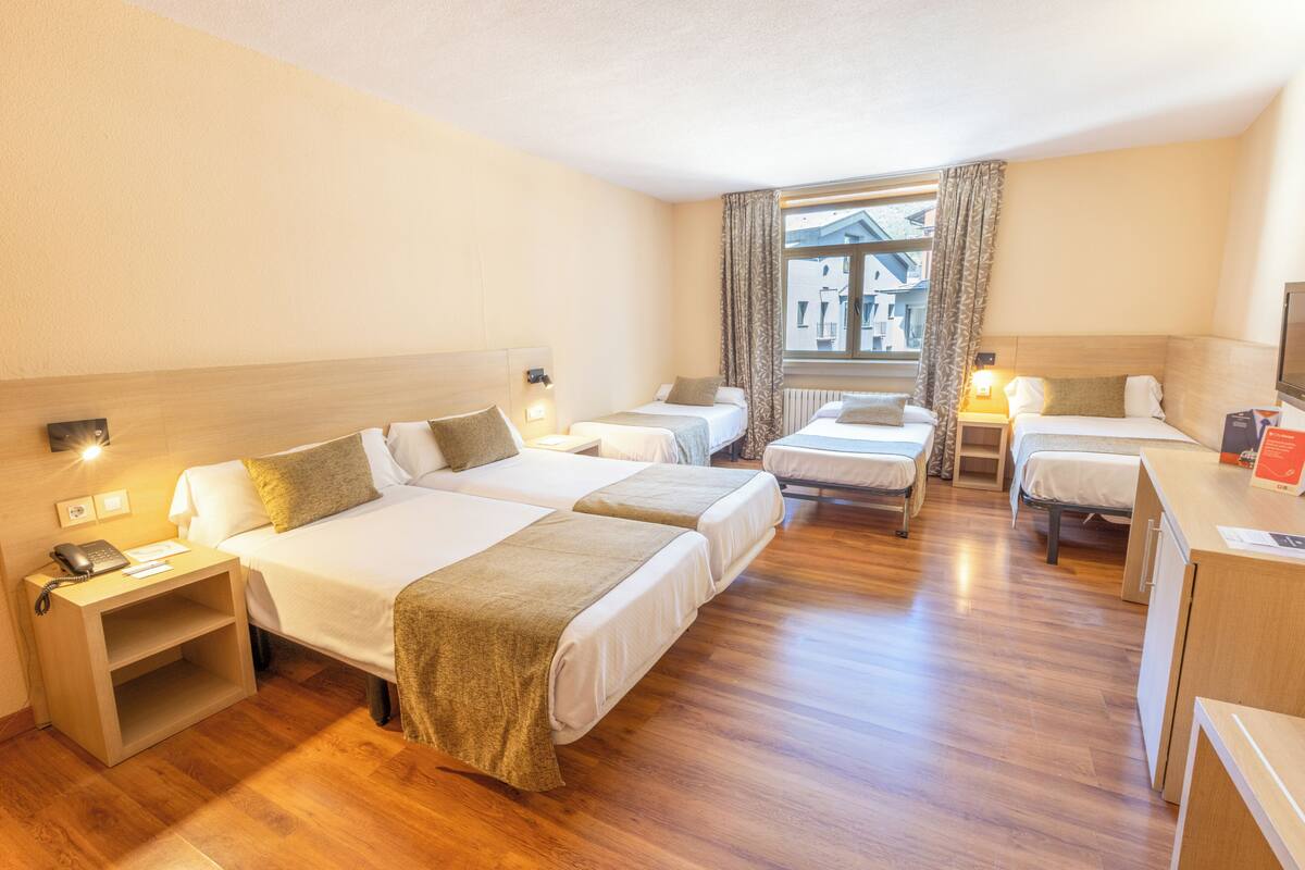 Quarto de hotel com três camas, uma escrivaninha, telefone e janela com cortinas.