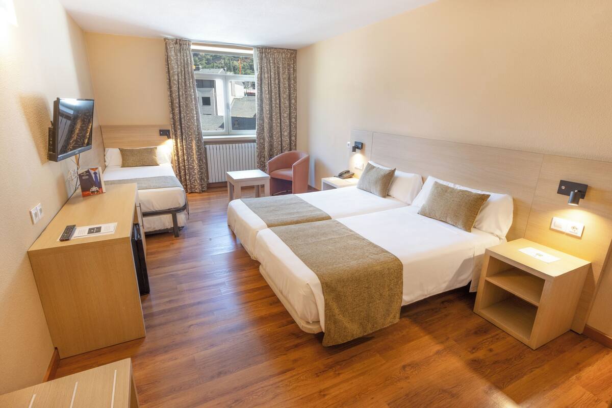 Quarto de hotel com duas camas, uma escrivaninha, uma cadeira, uma TV e uma janela com cortinas.