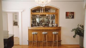 Uma área de bar com banquetas de madeira, balcão espelhado e um lustre.
