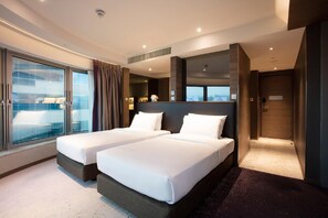 Quarto de hotel com duas camas, janelas amplas, vista para a cidade e uma porta escura.