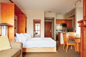 Quarto de hotel com cama, escrivaninha e cozinha compacta.