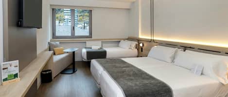 Quarto de hotel com cama, sofá, mesinha, televisão e janela vista para a cidade.