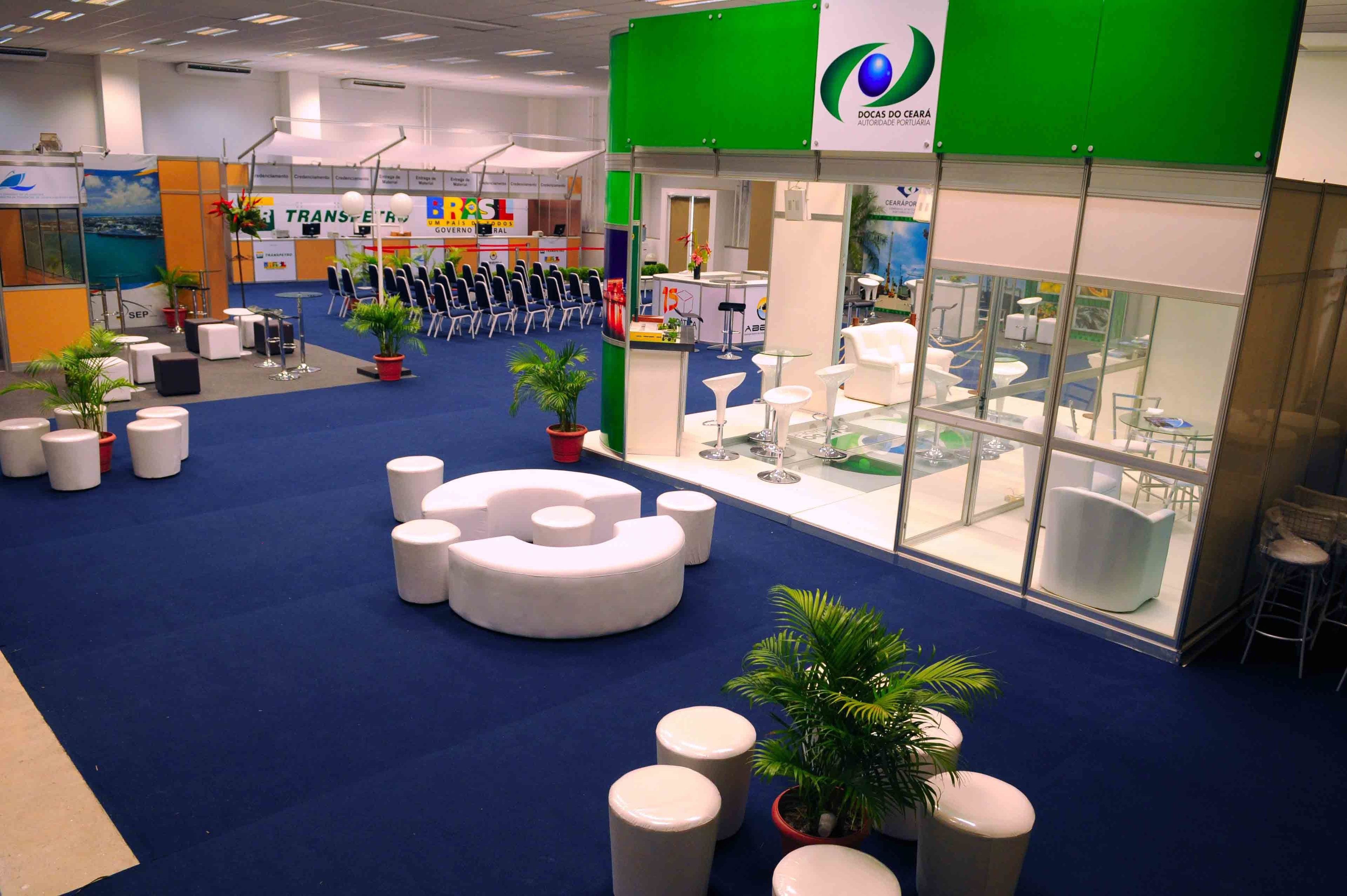 Um espaço amplo e interno, com carpete azul, assentos brancos e plantas em vasos.