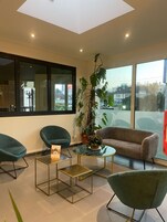 Uma sala de estar moderna com uma mesa de vidro, duas poltronas verdes, um sofá marrom e uma grande planta em vaso.