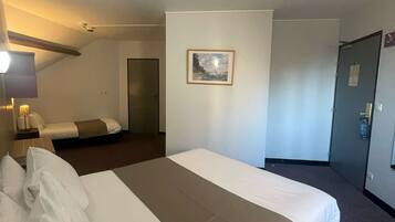 Quarto de hotel com uma cama grande, uma mesa de cabeceira com abajur, um quadro na parede e uma porta à direita.