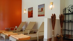 Um quarto de spa com cadeiras de lounge em vime, toalhas laranja e obras de arte penduradas na parede.