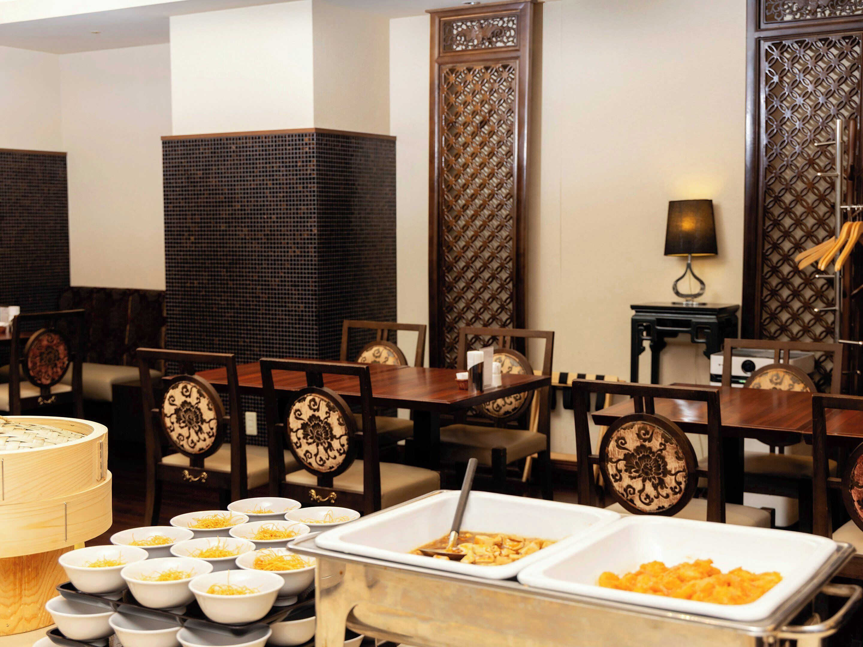 Disposição de buffet com várias tigelas de comida, cadeiras de madeira e um design de parede tradicional.
