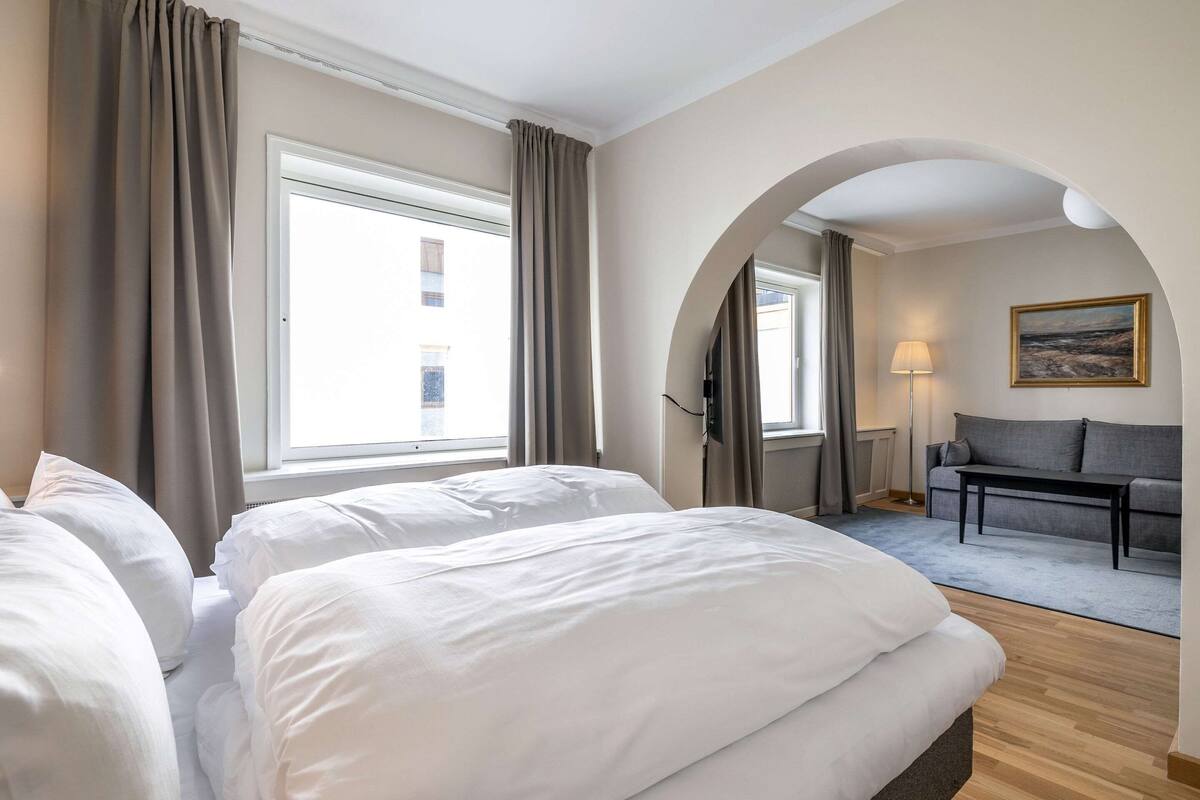 Quarto de hotel com duas camas, um sofá, uma luminária e um quadro na parede.