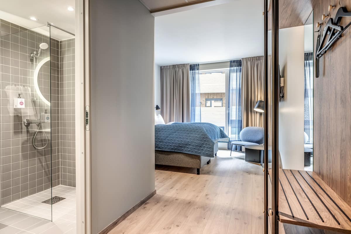 Quarto de hotel moderno com chuveiro, cama, área de estar e uma grande janela com cortinas.