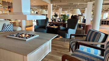 Um hall amplo com área de estar central, apresentando um recurso de fogo, poltronas confortáveis e um bar com diversas garrafas.