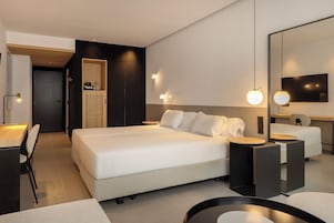 Quarto de hotel moderno com uma cama grande, mesas de cabeceira, um guarda-roupa, uma escrivaninha e uma televisão.