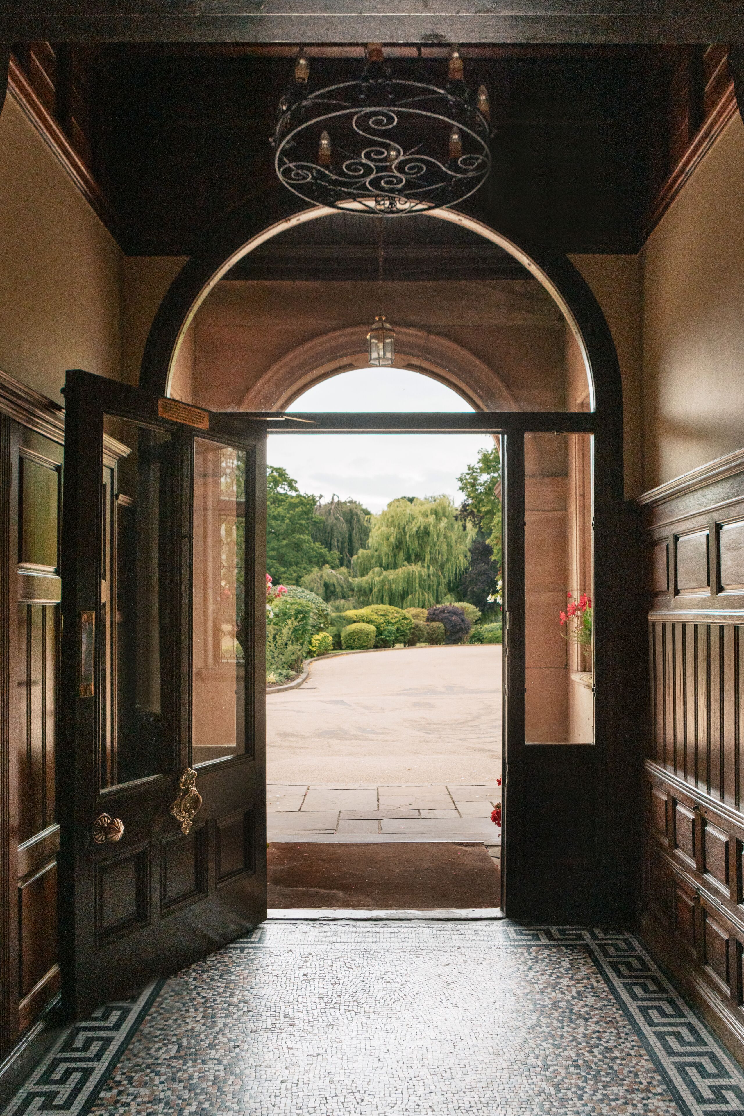 Uma porta em arco que dá para um pátio com piso de azulejos e vista para o verde.