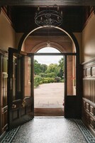 Uma porta em arco que dá para um pátio com piso de azulejos e vista para o verde.