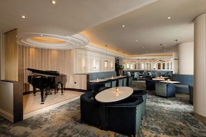 Um hall de hotel espaçoso com um piano de cauda, assentos confortáveis e um lustre moderno.