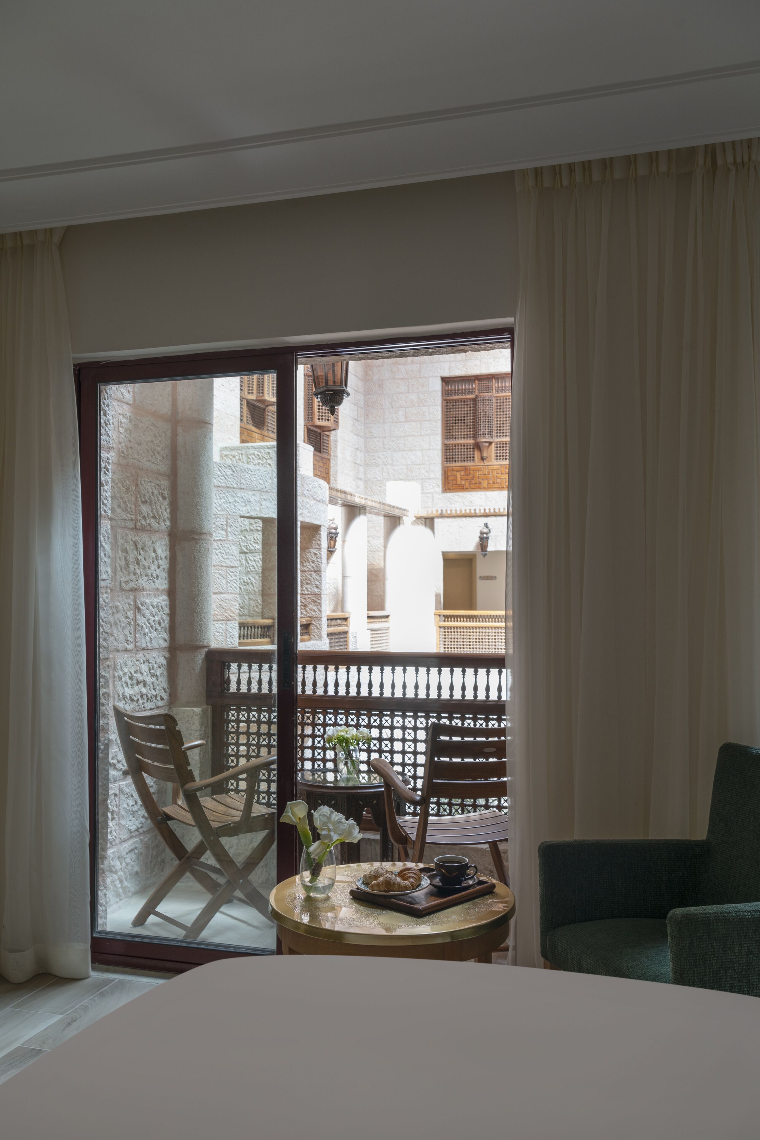 Quarto com varanda, mesa com um vaso de flores e duas cadeiras.