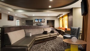 Um hall de hotel moderno com sofá, poltronas, uma mesinha e uma TV fixada na parede.