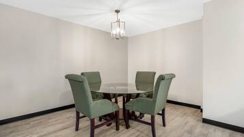 Uma sala de conferências com uma mesa redonda, quatro cadeiras estofadas verdes, um candelabro e paredes em tons claros.