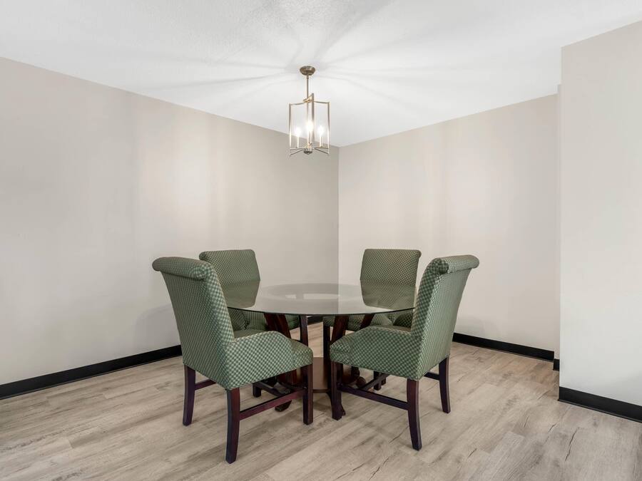 Uma sala de conferências com uma mesa redonda, quatro cadeiras estofadas verdes, um candelabro e paredes em tons claros.