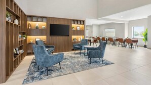 Um hall amplo com uma grande TV de tela plana, estantes de madeira com objetos decorativos e uma área de estar com cadeiras azuis.