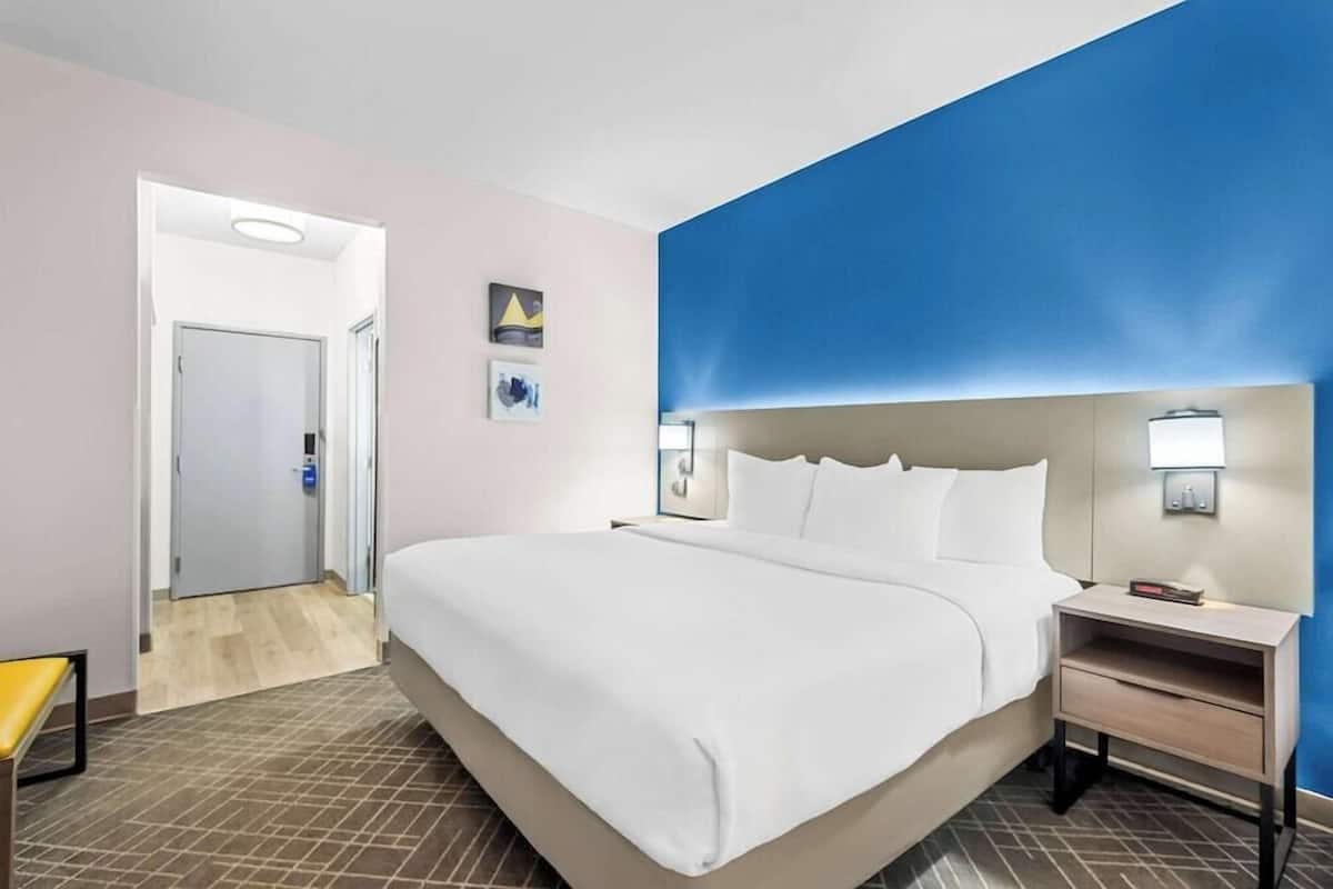Quarto de hotel com uma cama grande, uma mesa de cabeceira e uma porta, com uma parede destacada em azul.